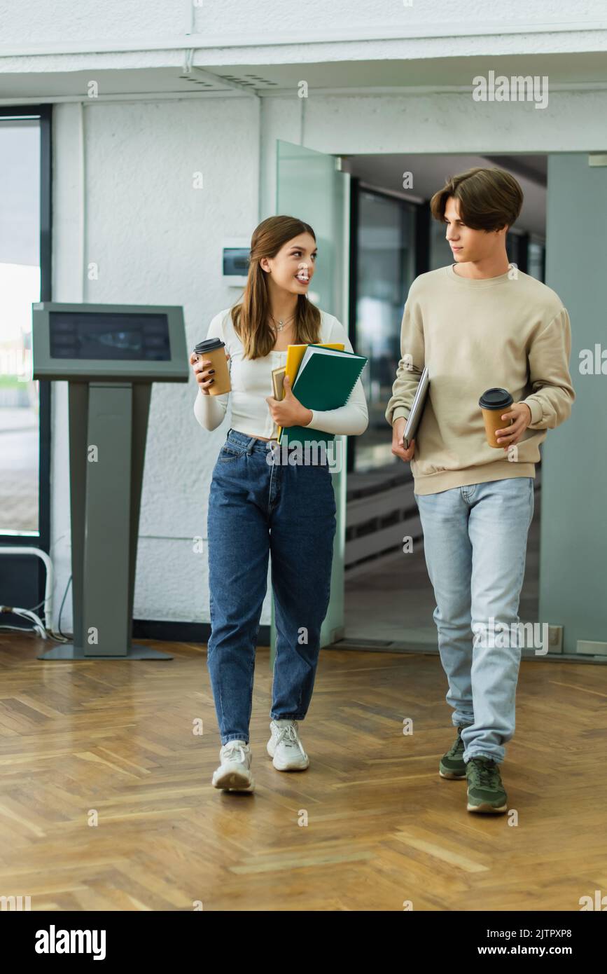 smiling teenage girl with notebooks talking to friend with laptop while ...