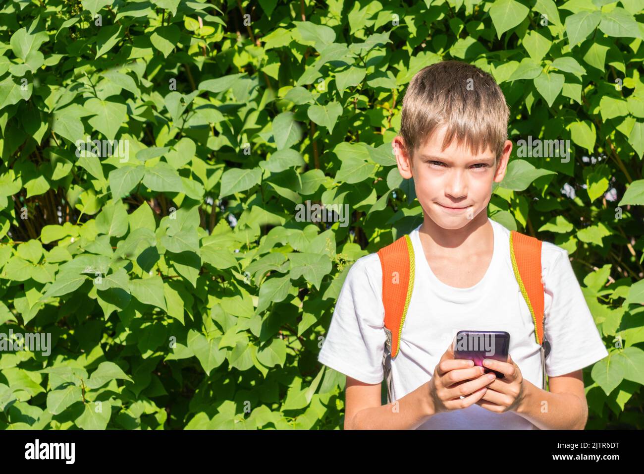 Portrait of a happy schoolboy with a backpack using a smartphone ...