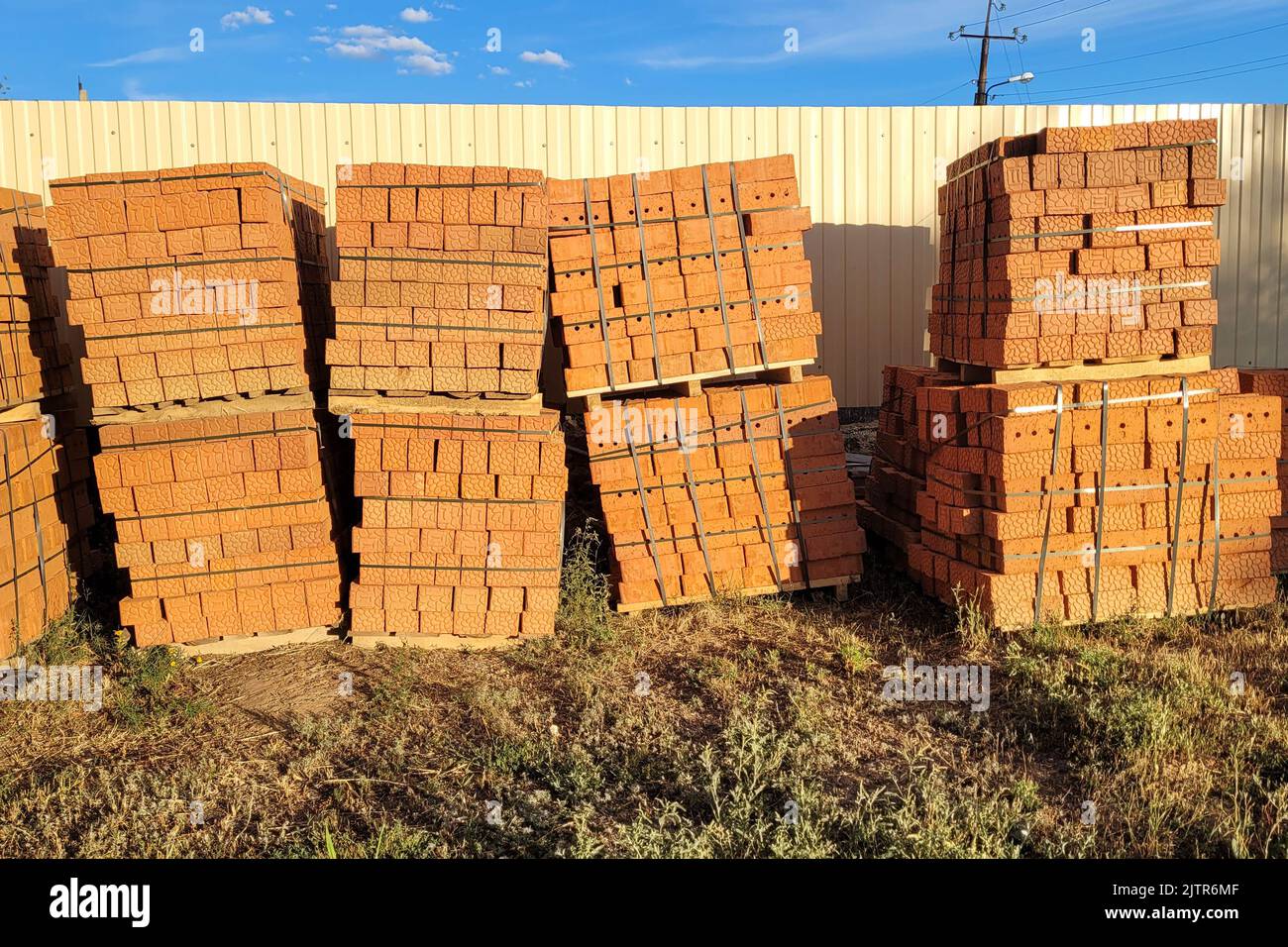 Brown bricks stacked on pallets along construction site fence Stock ...