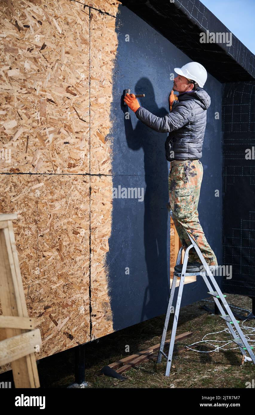 Male painter using paint roller, doing exterior paint work in a black ...