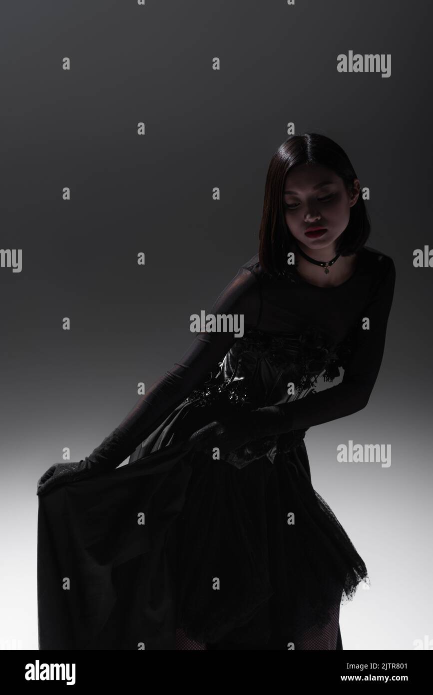young asian woman in black gothic dress holding lace skirt while posing ...