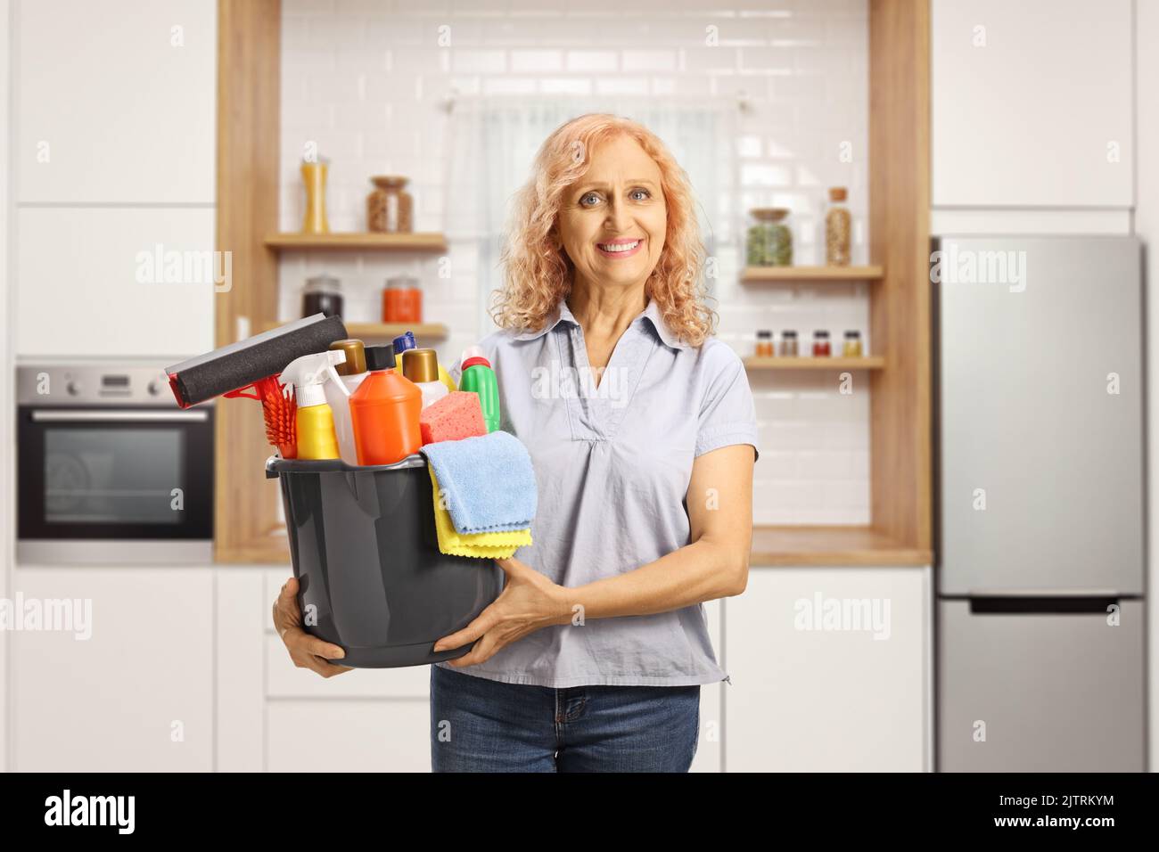 Mature woman holding a bucket with cleaning supplies inside a modern ...