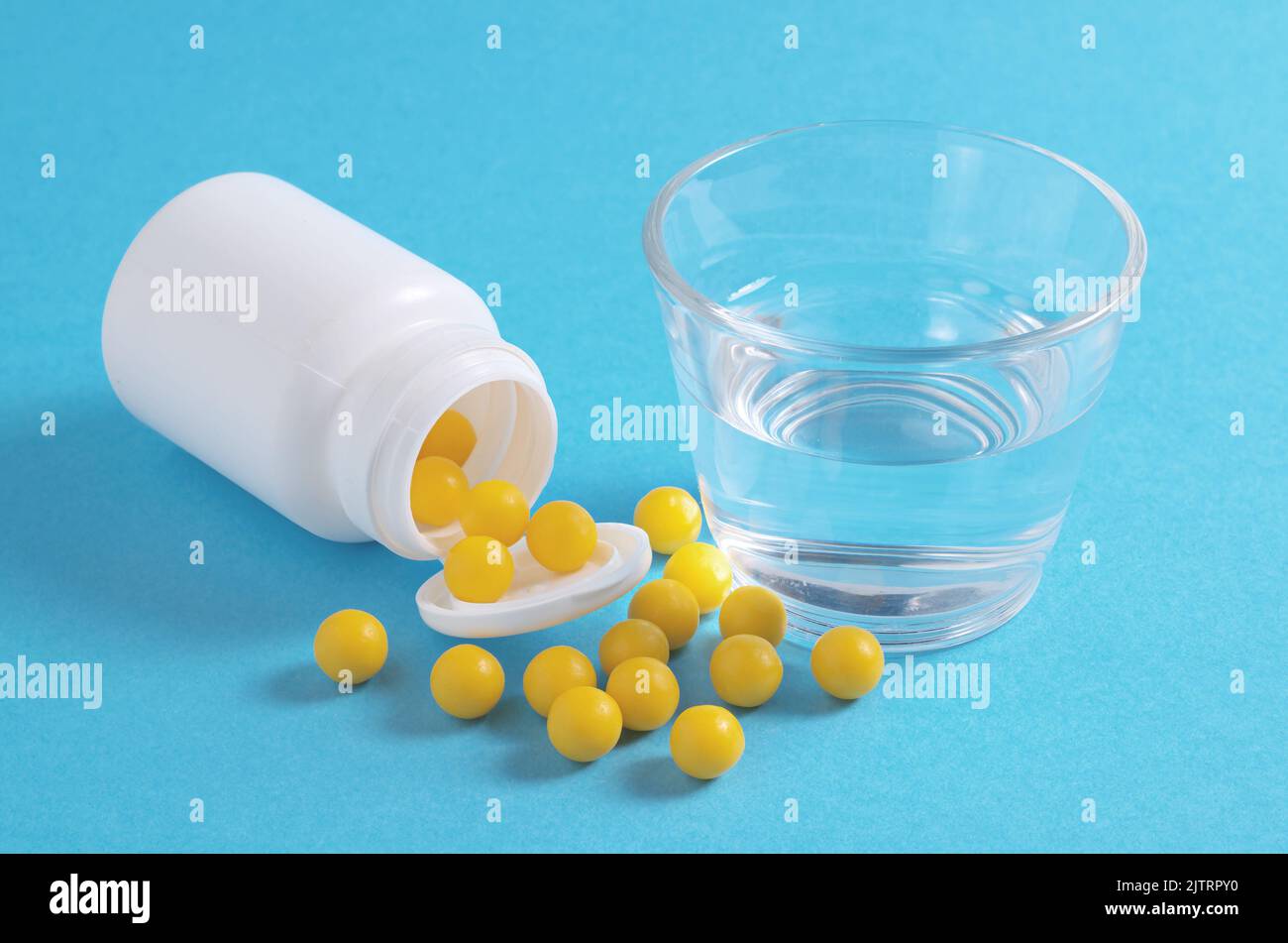 Yellow vitamin pills and white plastic bottle pack and glass of water ...
