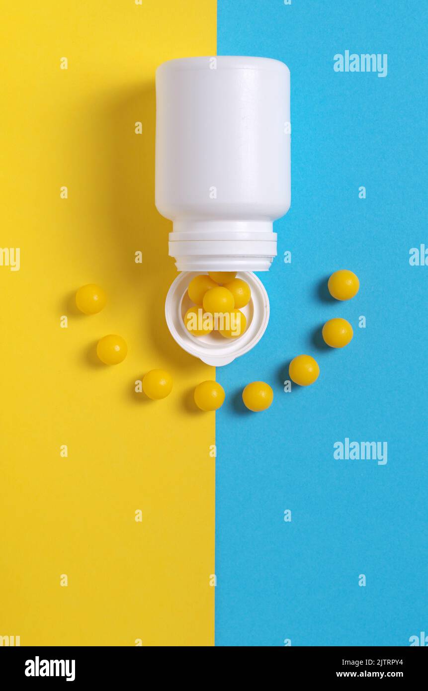 Yellow vitamin pills and white plastic bottle pack on two-tone ...