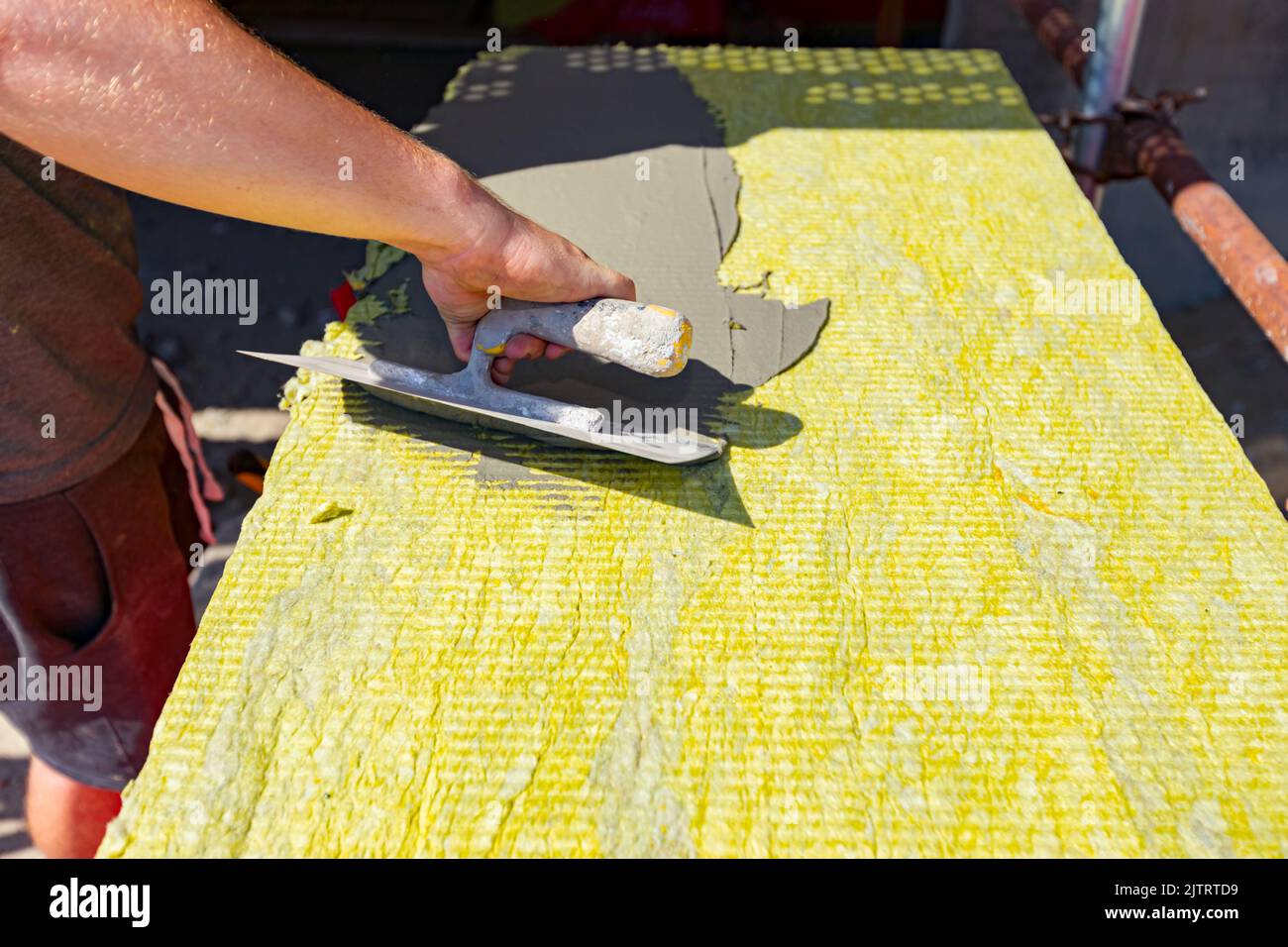 View on worker's hand with trowel, applying glue on yellow mineral wool ...