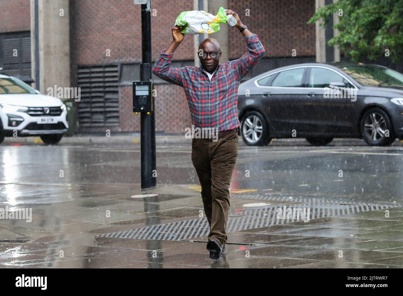 A man shelters under a shopping bag during rainfall in London Stock ...