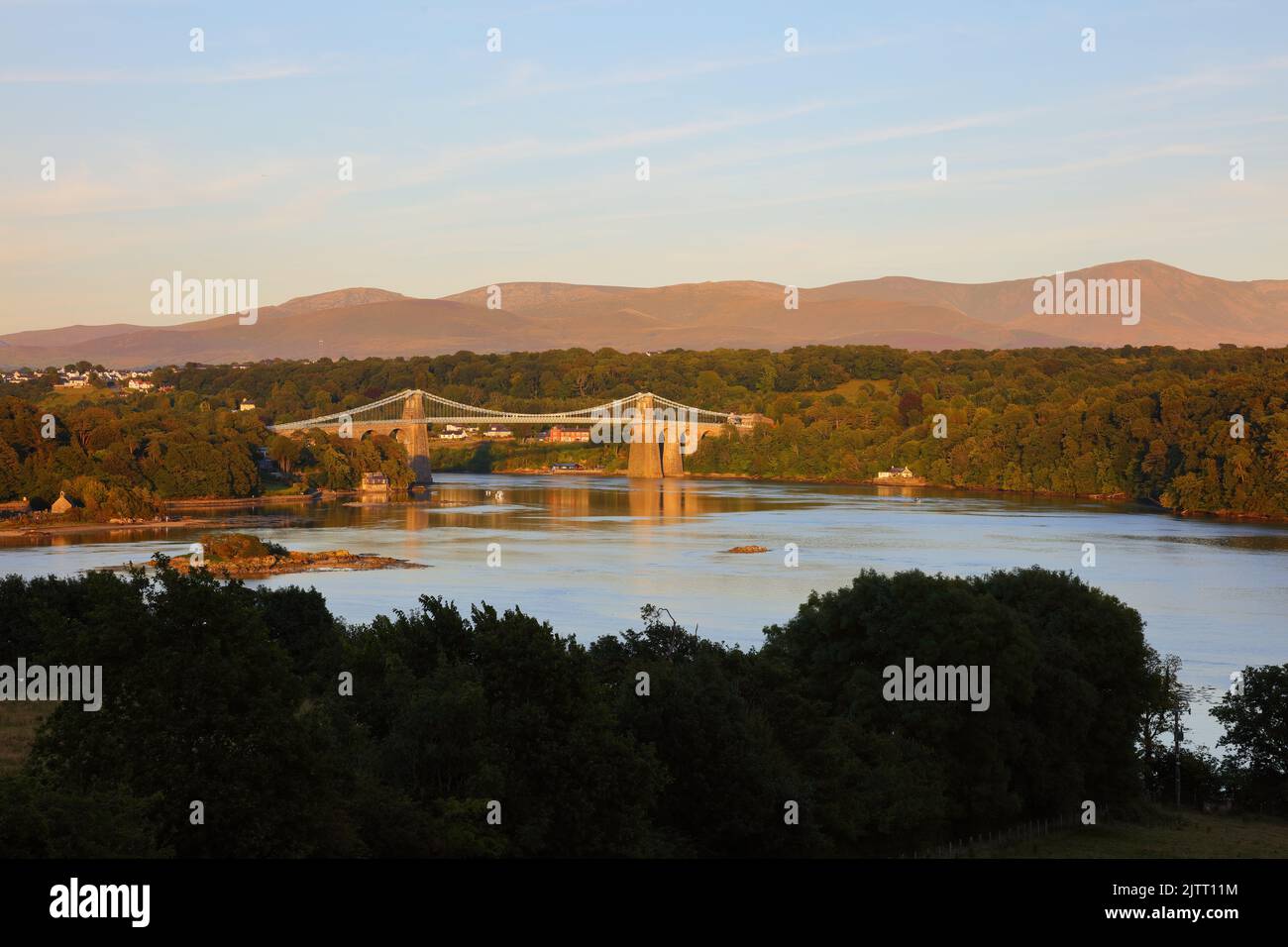 The Menai Suspension Bridge bathed in warm evening light with Snowdonia ...