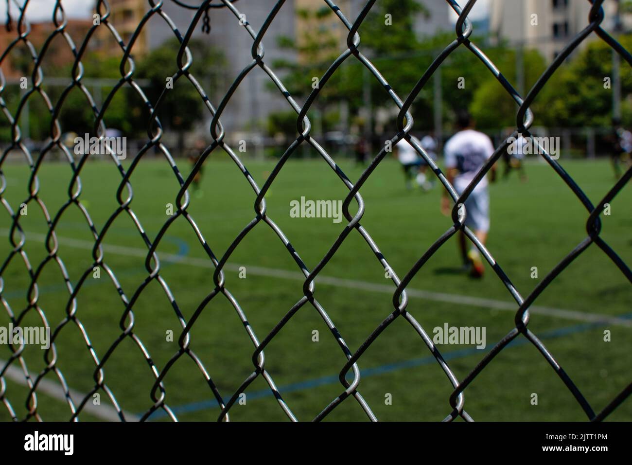 A closeup of mesh wire fence of football field with players in the blur ...
