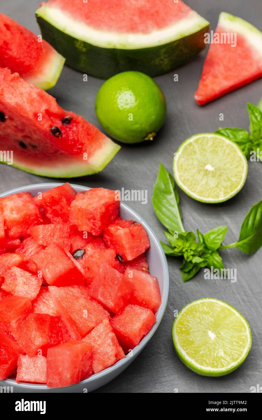 Watermelon slices, lime halves and sprig of basil on table. Sliced ...