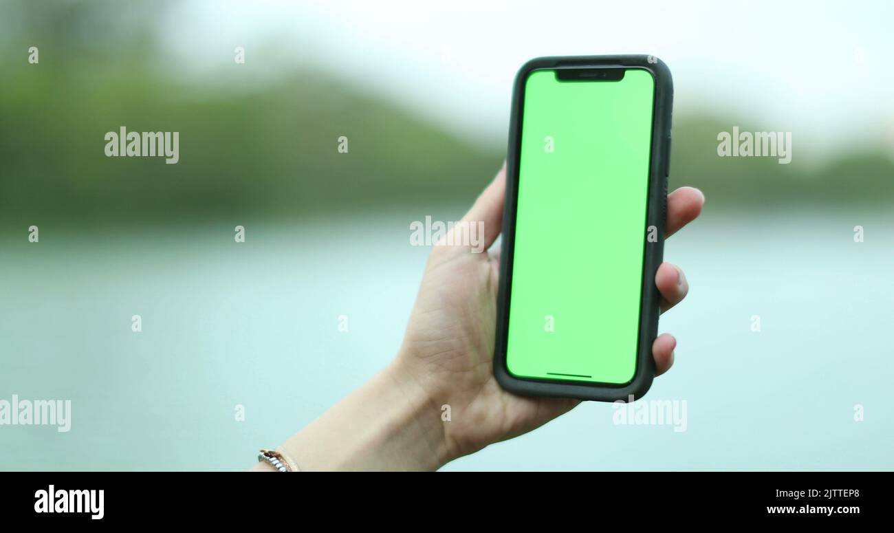 Hand holding smartphone device with greenscreen. Chroma key, close up woman hand holding phone ...