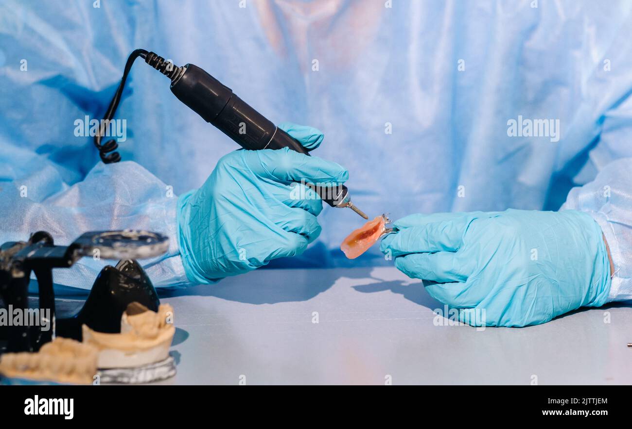 A masked and gloved dental technician works on a prosthetic tooth in ...