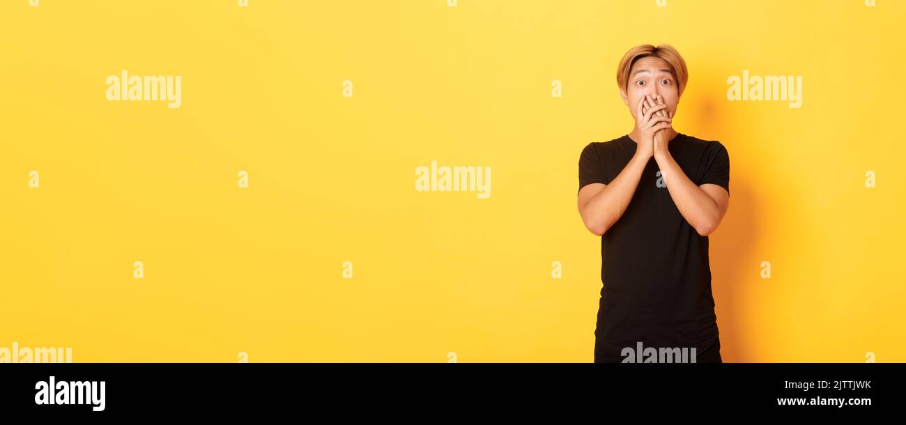 Portrait of surprised asian handsome guy with blond hair, cover mouth ...