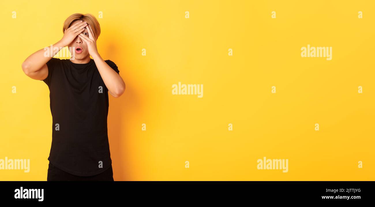 Portrait of embarrassed asian guy with blond hair, gasping startled and ...
