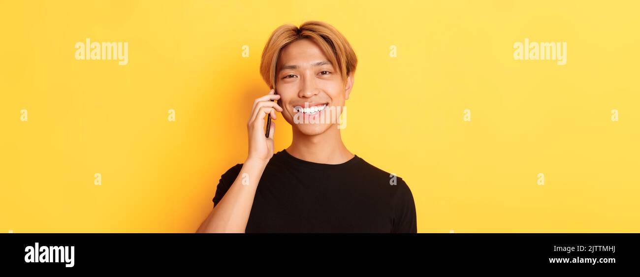 Close-up of handsome stylish korean guy smiling and talking on mobile ...