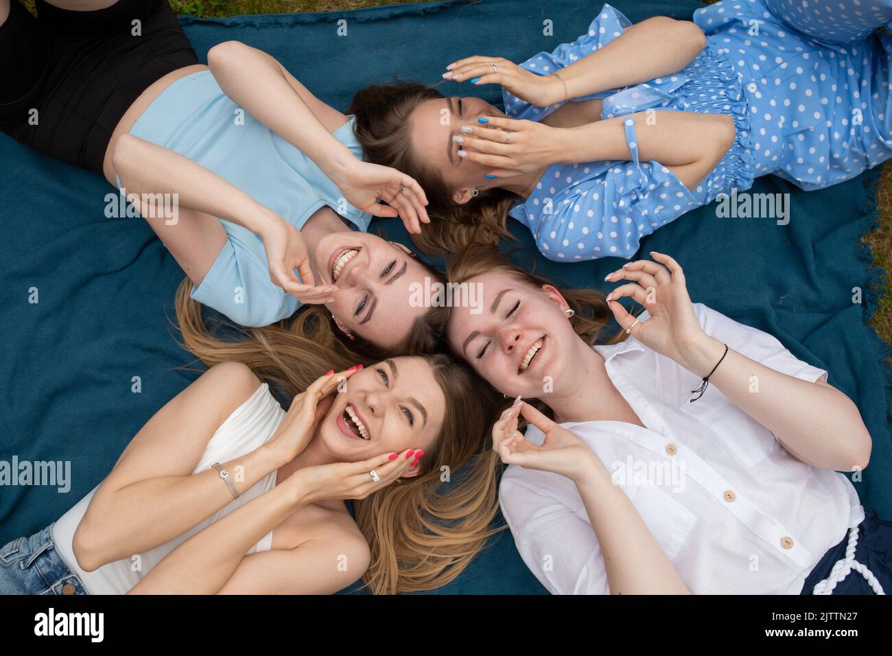 Top view of young laughing women raising hands to face, lying in circle ...