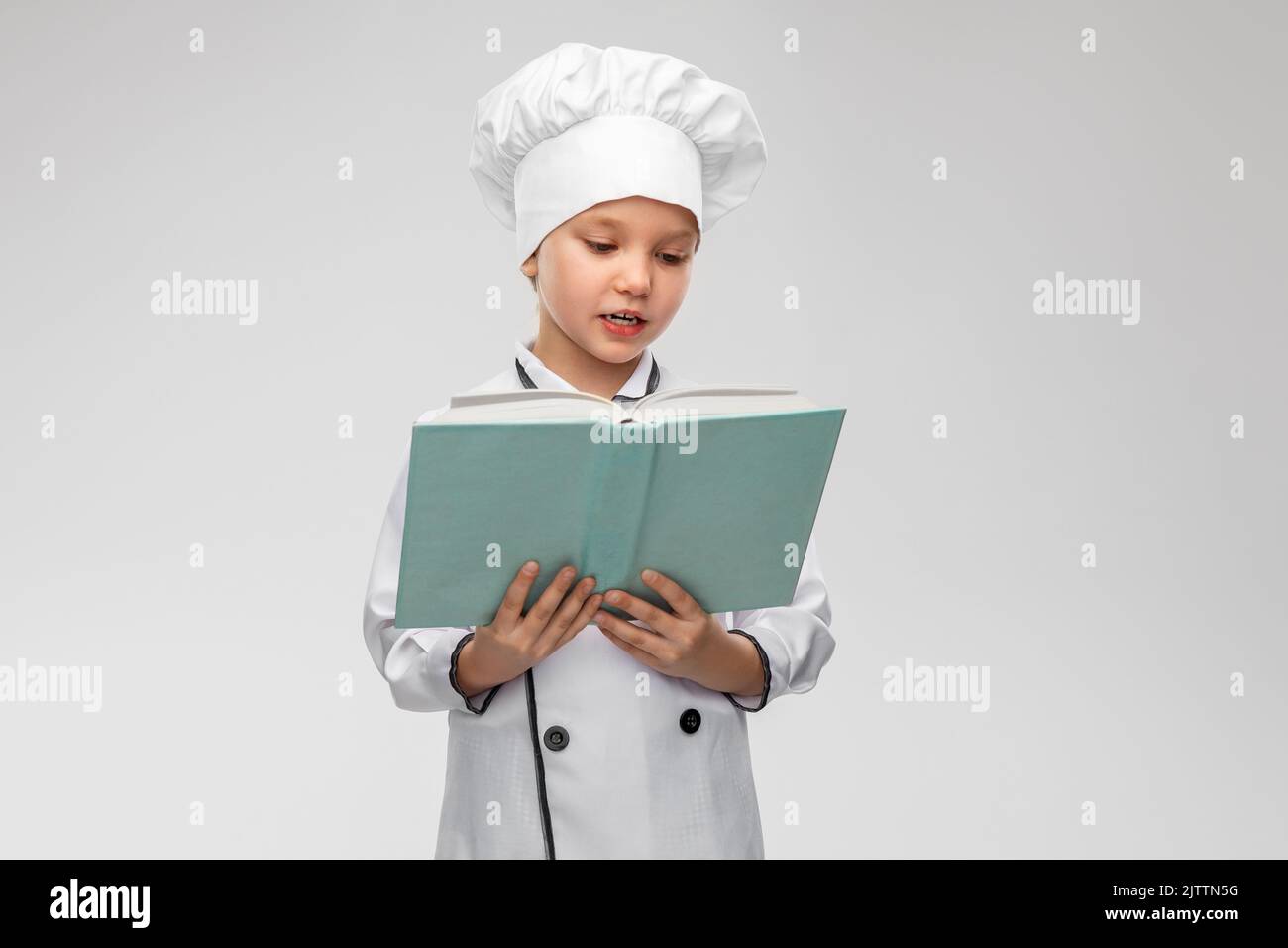 little girl in chef's toque reading cook book Stock Photo - Alamy