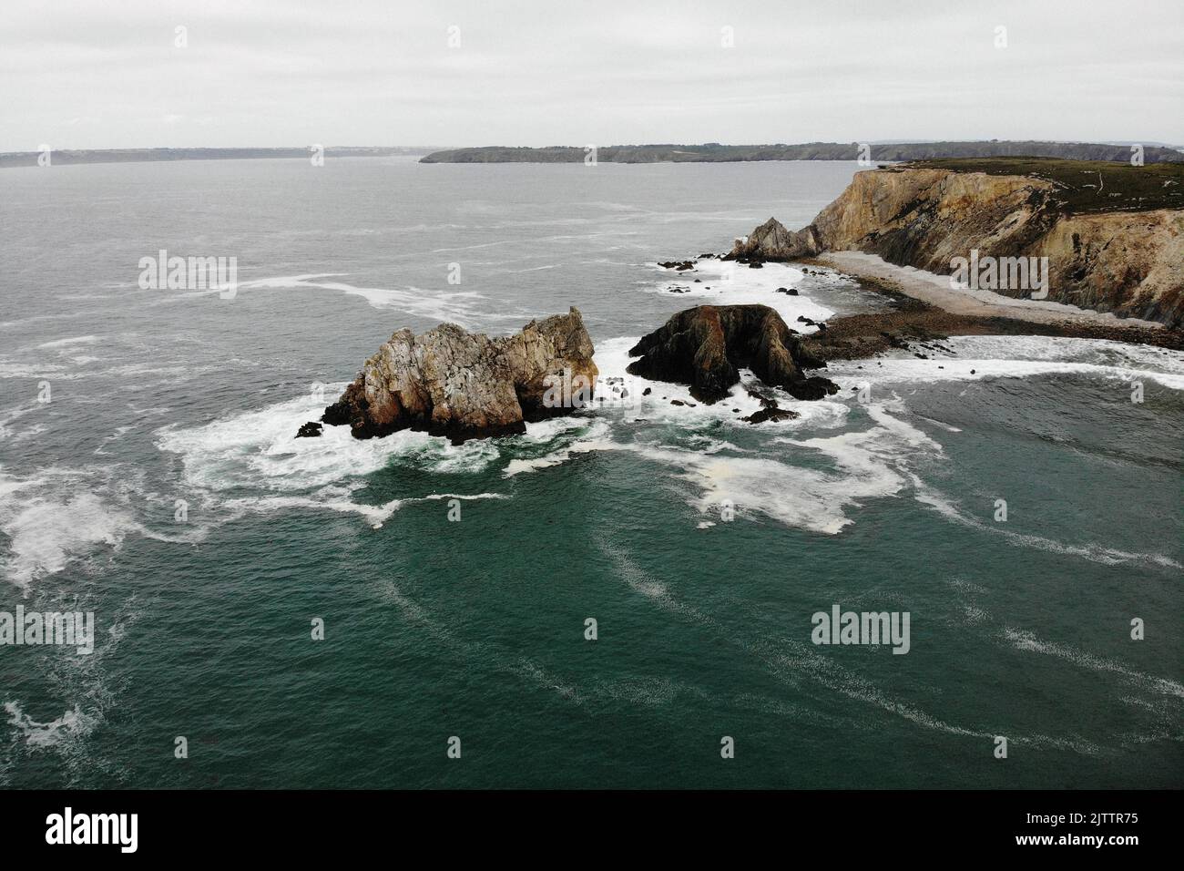 A drone shot of a seascape with waves crashing huge rocks and a cliff ...