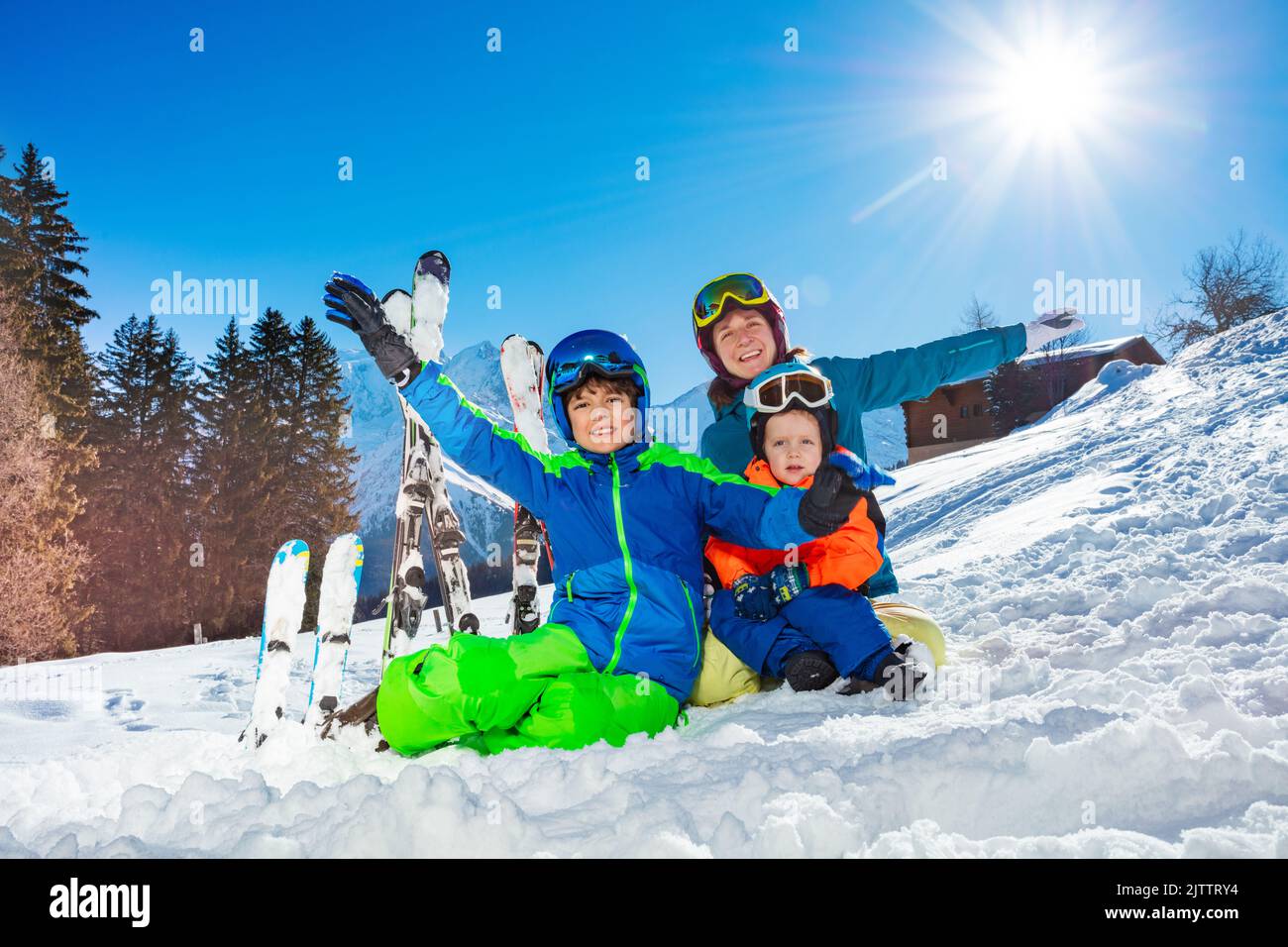 Two kids and mother on ski vacation sit in the snow over Alps Stock ...