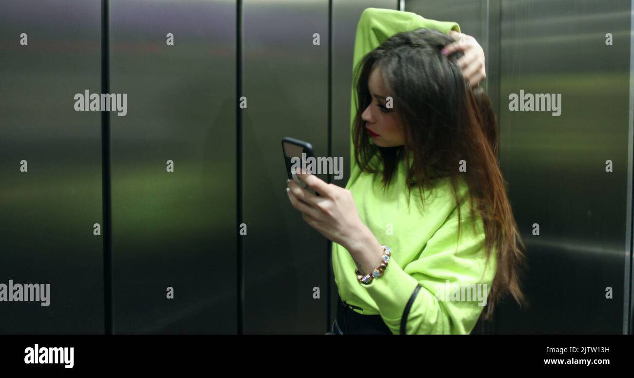 Pretty girl adjusting hair taking photo in front of mirror at elevator ...