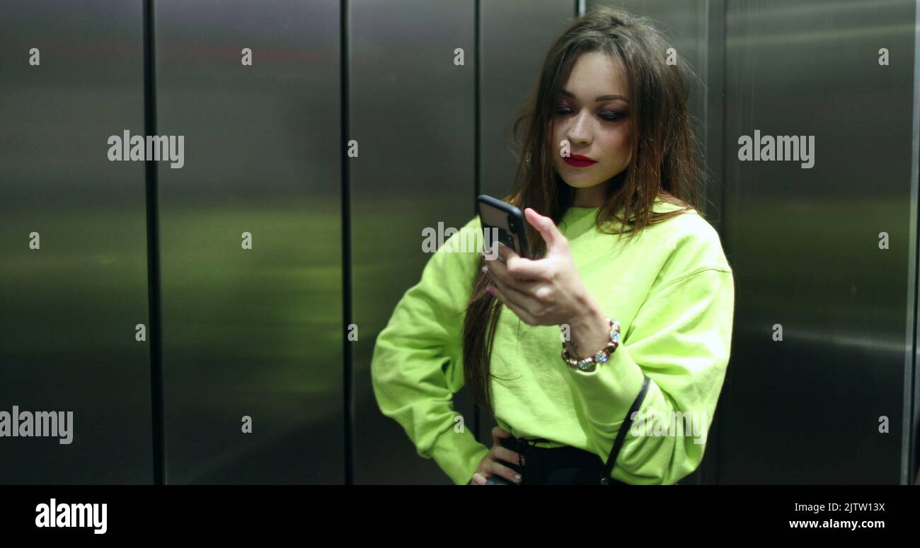 Pretty girl adjusting hair taking photo in front of mirror at elevator ...