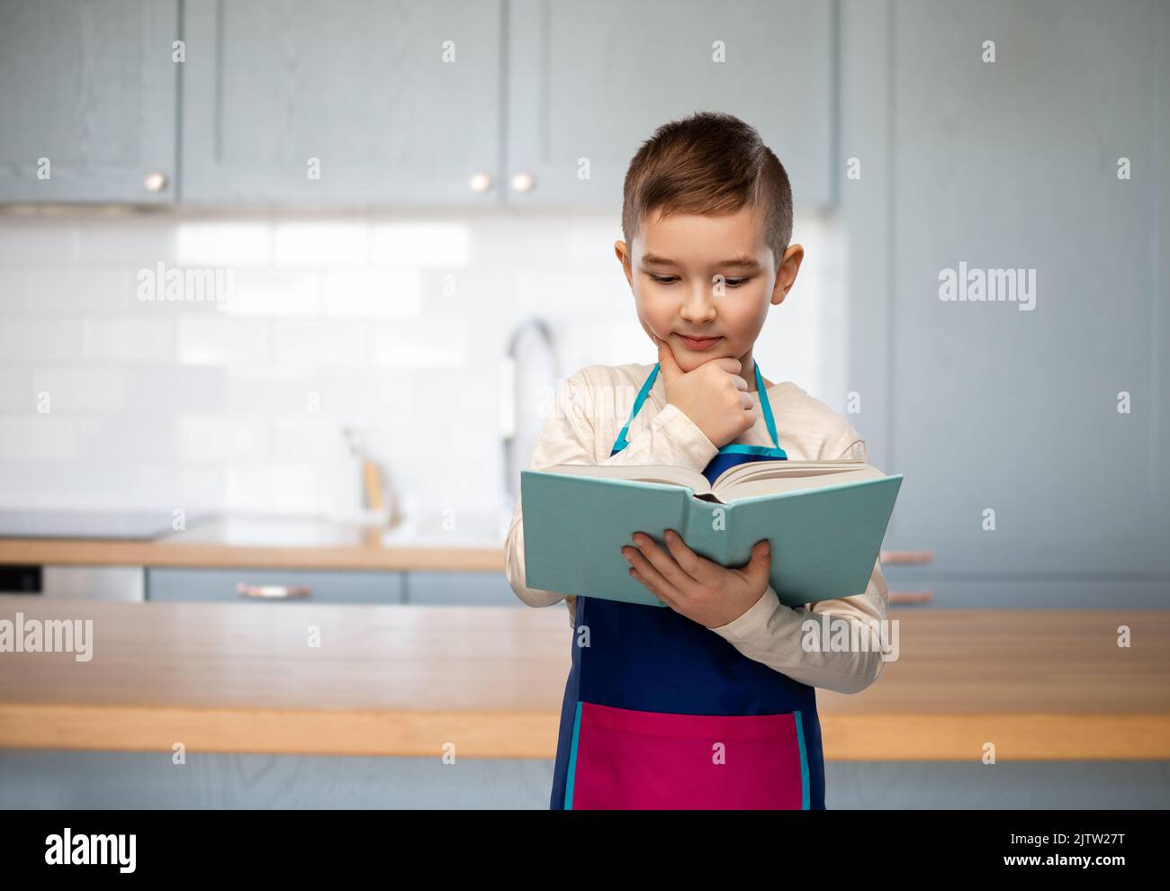 little boy in apron reading cook book and thinking Stock Photo - Alamy