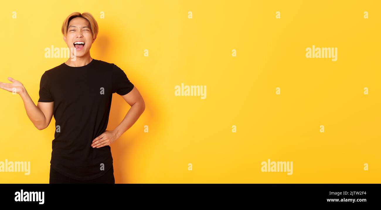 Portrait of happy blond asian guy, winking sassy and smiling, holding ...
