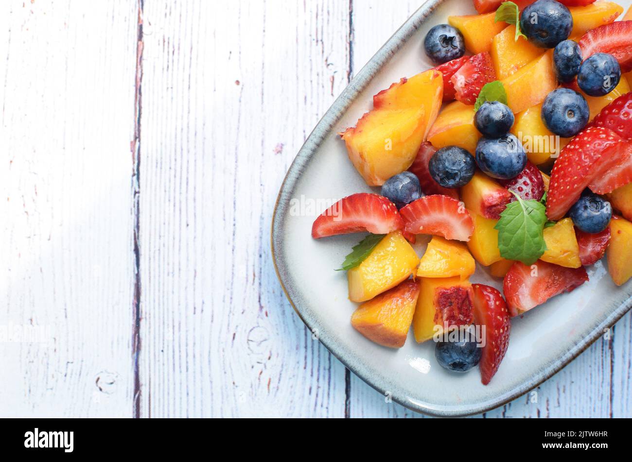 Fruit salad in a rectangular plate on a white wooden background. Sliced ...