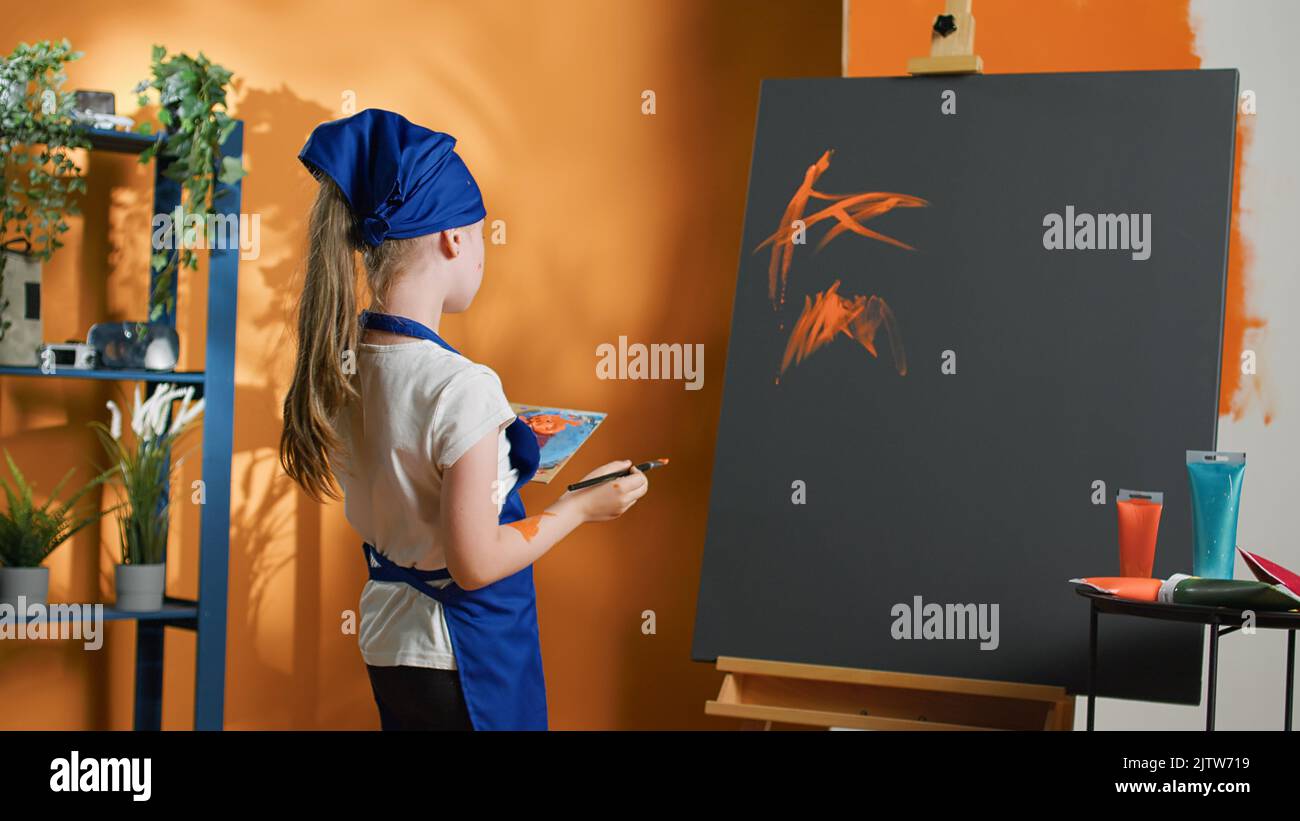Young child painting masterpiece with orange color and paintbrush ...
