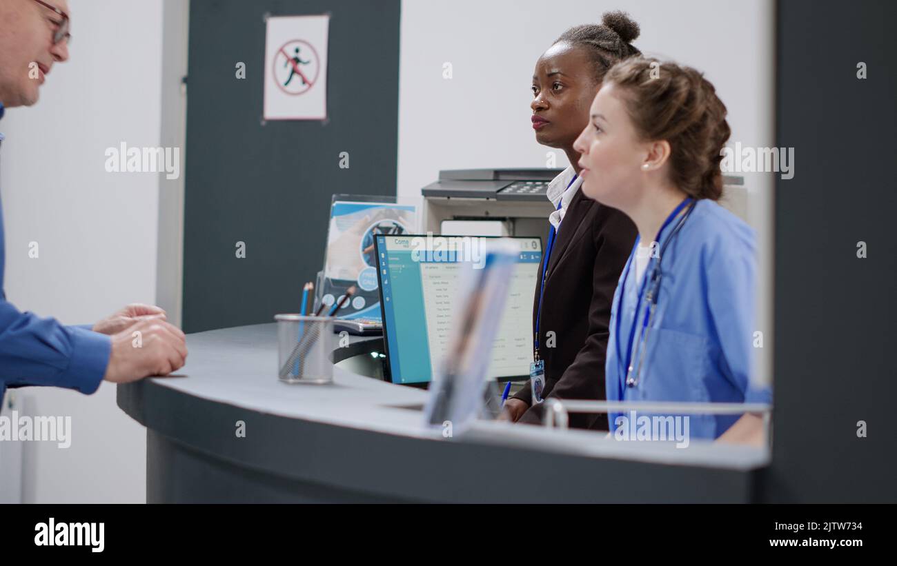 Diverse medical staff working at hospital reception counter, helping ...