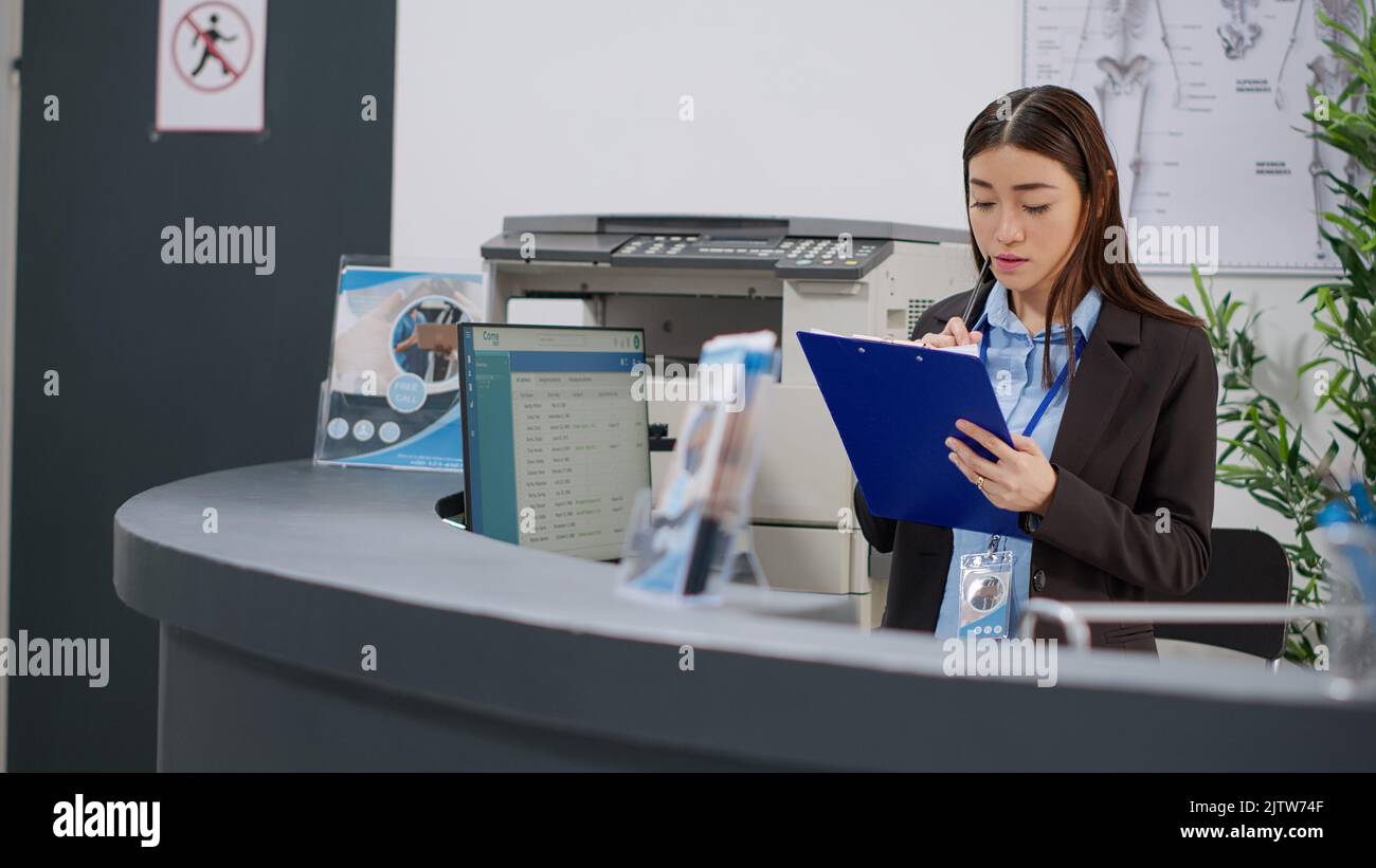 Woman receptionist working on healthcare appointments with checkup report papers at hospital ...