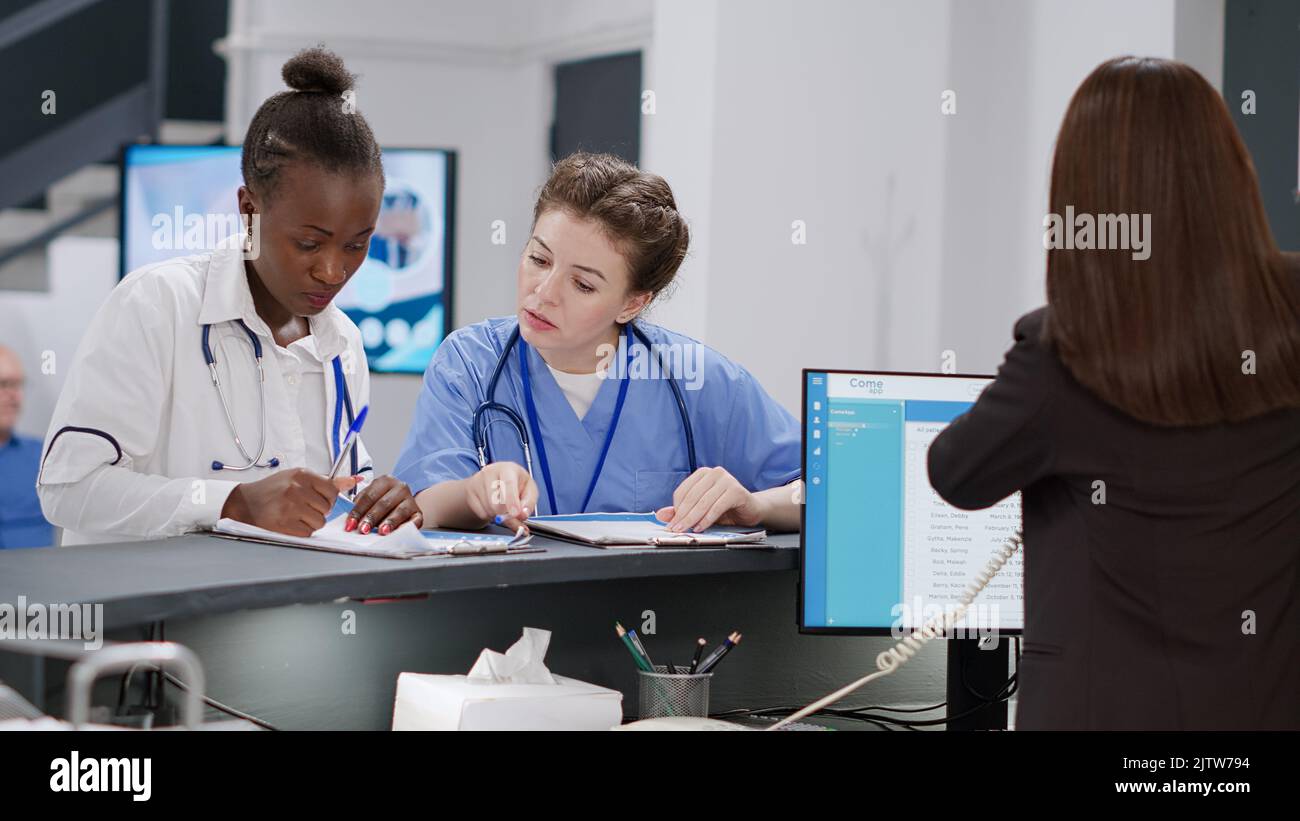 Diverse medical team working at hospital reception desk ith ...