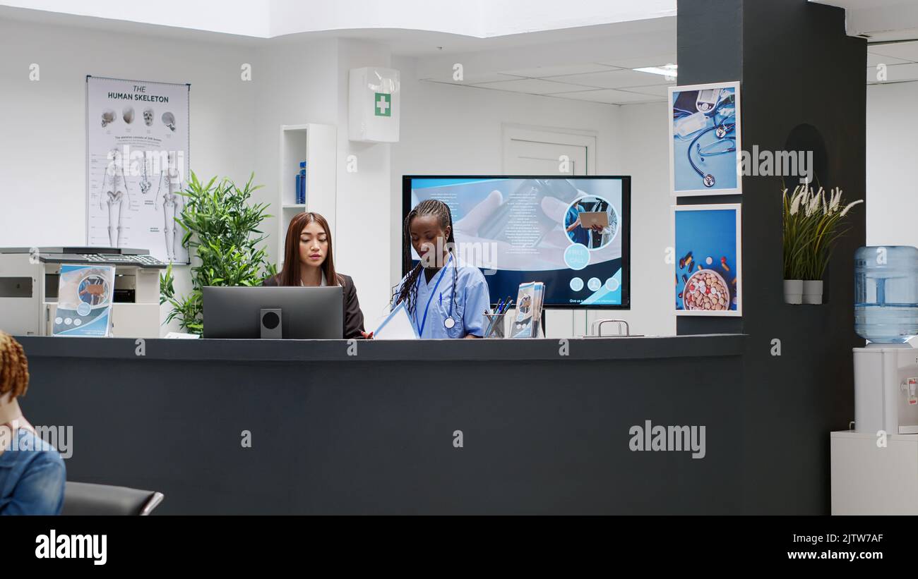 Diverse medical team working at hospital reception desk, giving ...