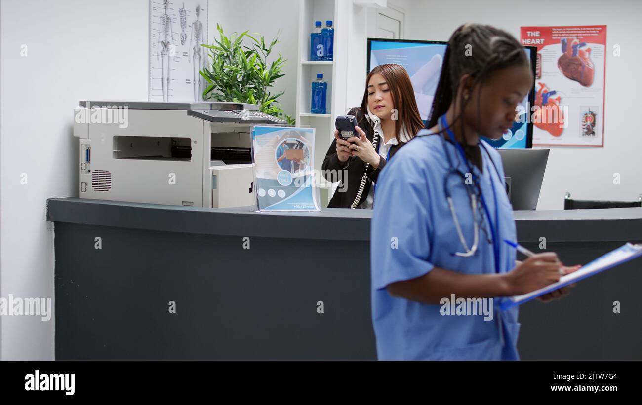 Asian receptionist answering landline phone call to help with checkup ...