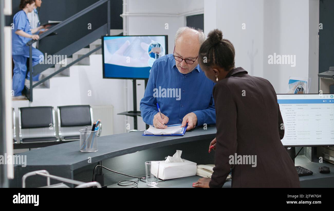 Old patient filling in medical report papers at registration desk ...