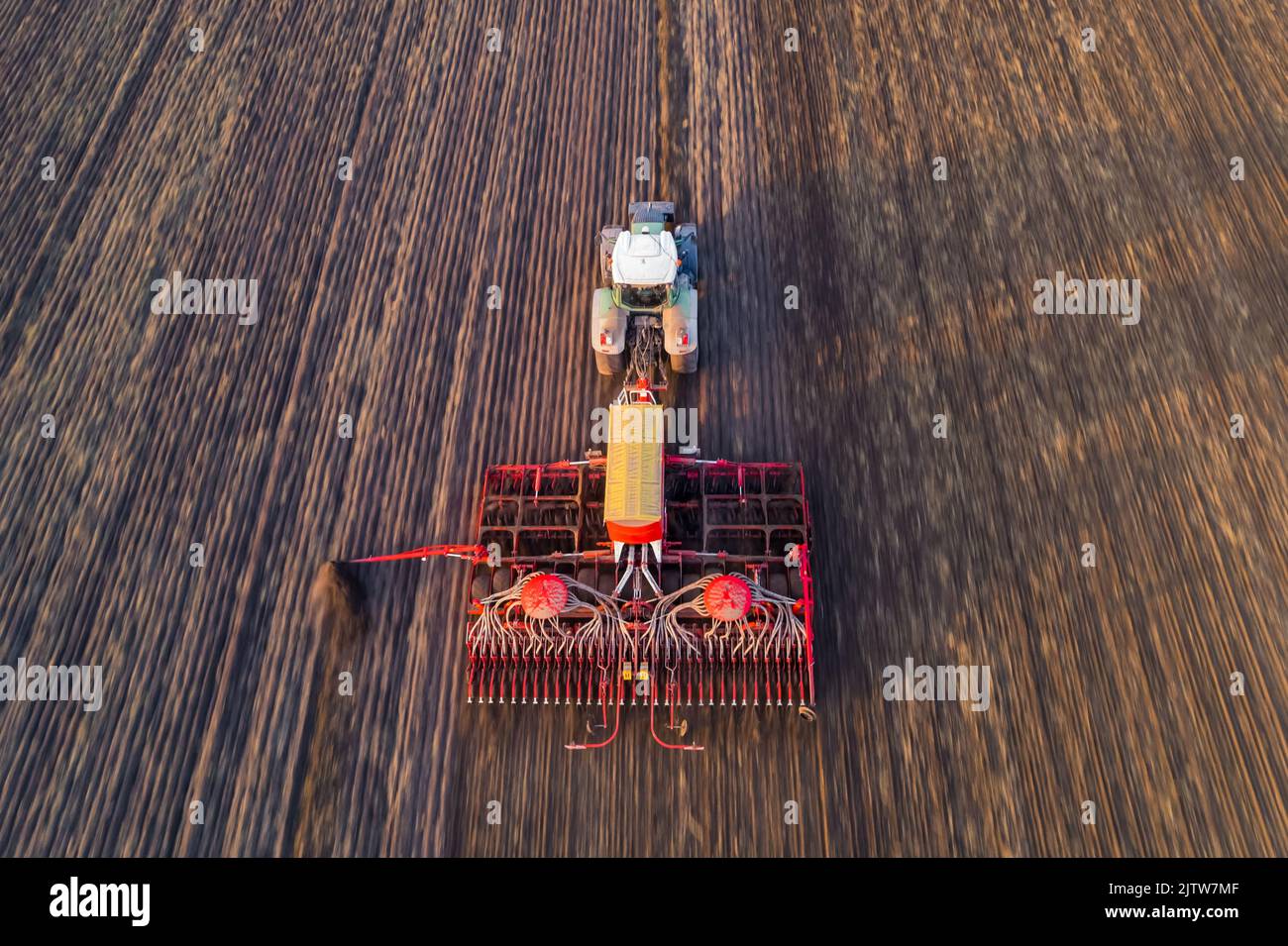 Top-down view of tractor with sowing machine driving through brown ...
