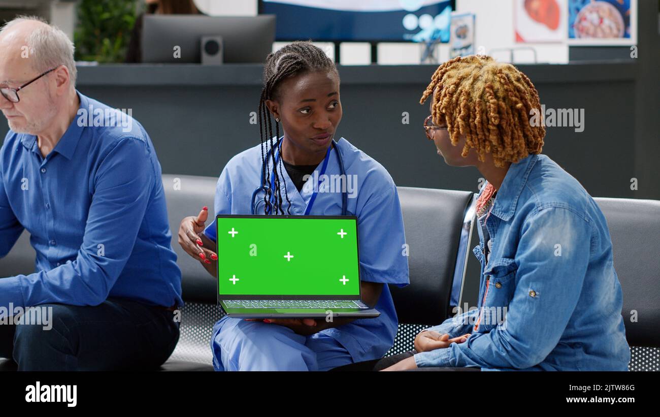 Medical assistant showing laptop with greenscreen to young patient in ...