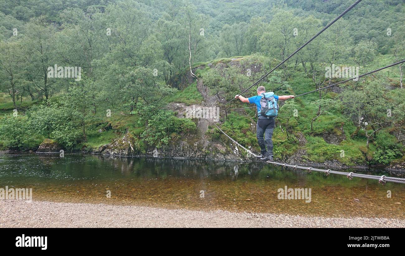 A man walking on a rope over a river surrounded by a forest in daylight ...