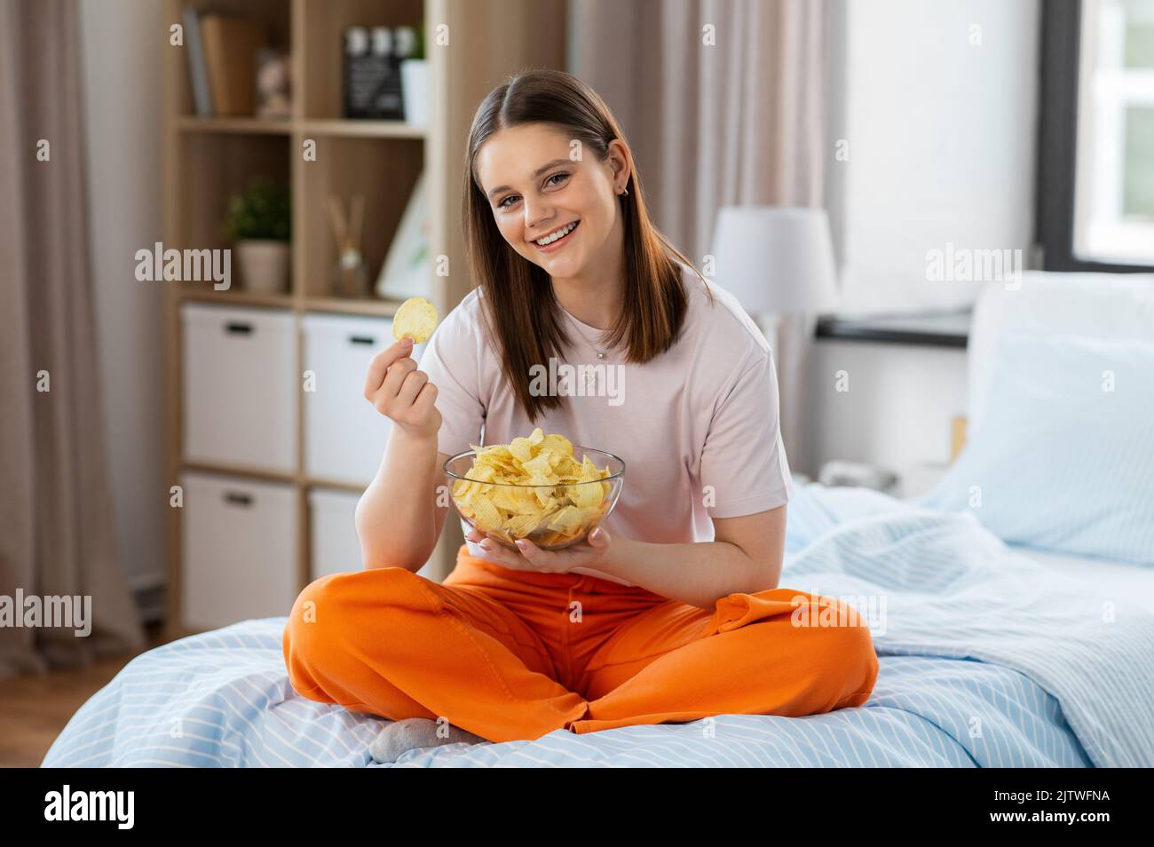 happy girl eating crisps sitting on bed at home Stock Photo - Alamy
