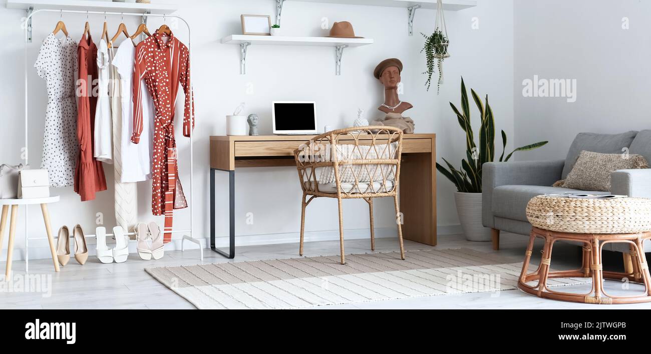 Interior of light room with workplace and rack with female clothes ...