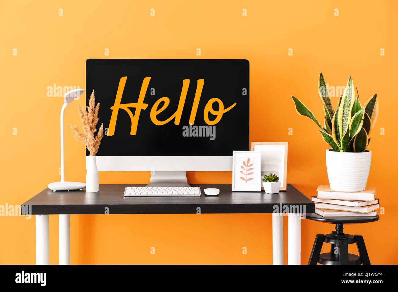 Modern computer with word HELLO on screen at workplace near orange wall ...