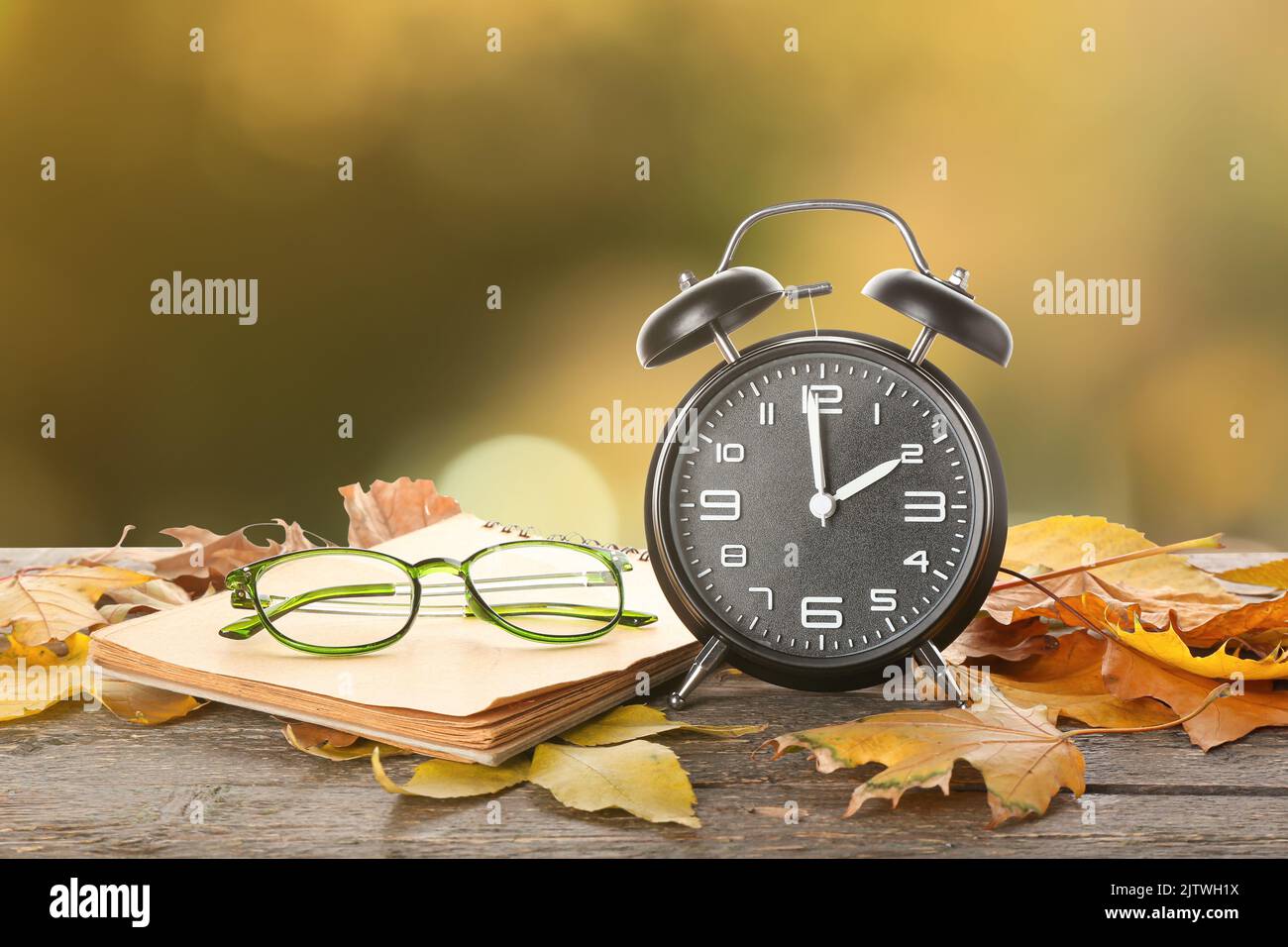 Alarm clock with notebook, eyeglasses and autumn leaves on wooden table ...
