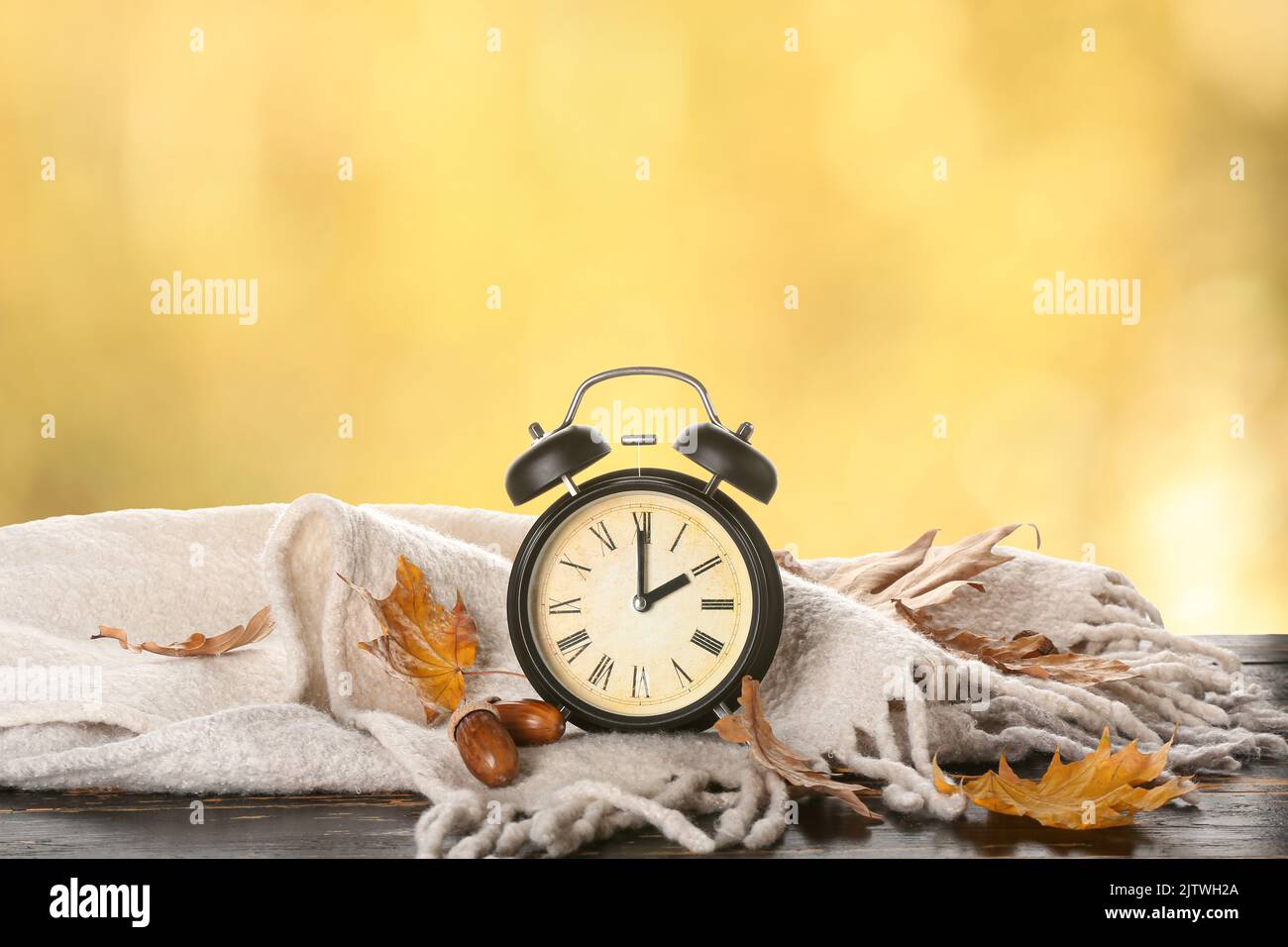 Alarm clock with knitted plaid and autumn leaves on wooden table ...