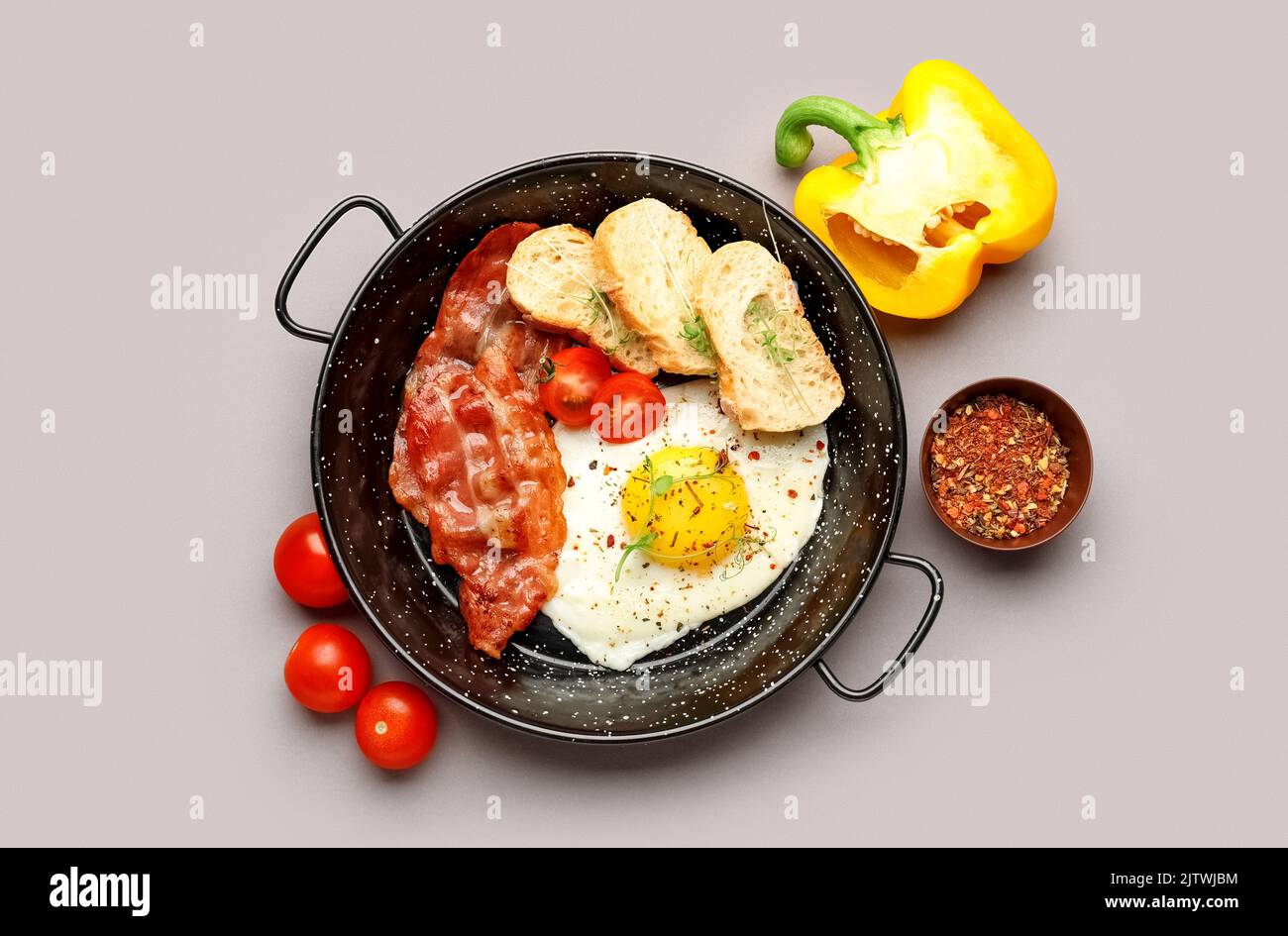 Frying pan with tasty fried egg, bacon, bread, vegetables and spices on ...