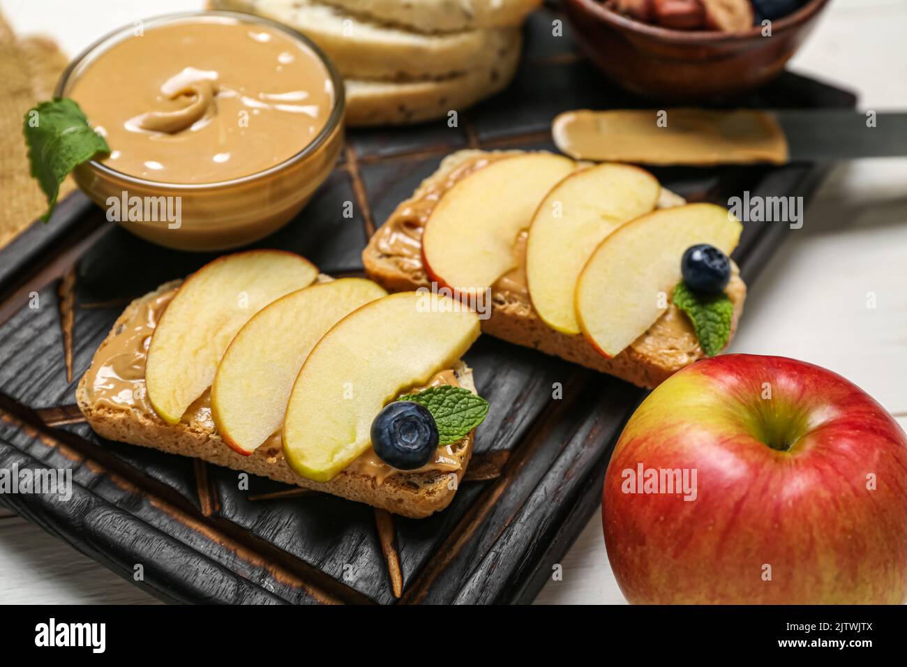 Wooden board of tasty sandwiches with nut butter and apples on table ...