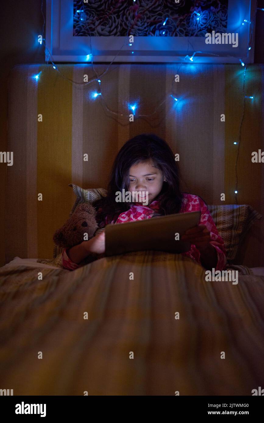 All settled in with a digital bedtime story. a little girl using a ...