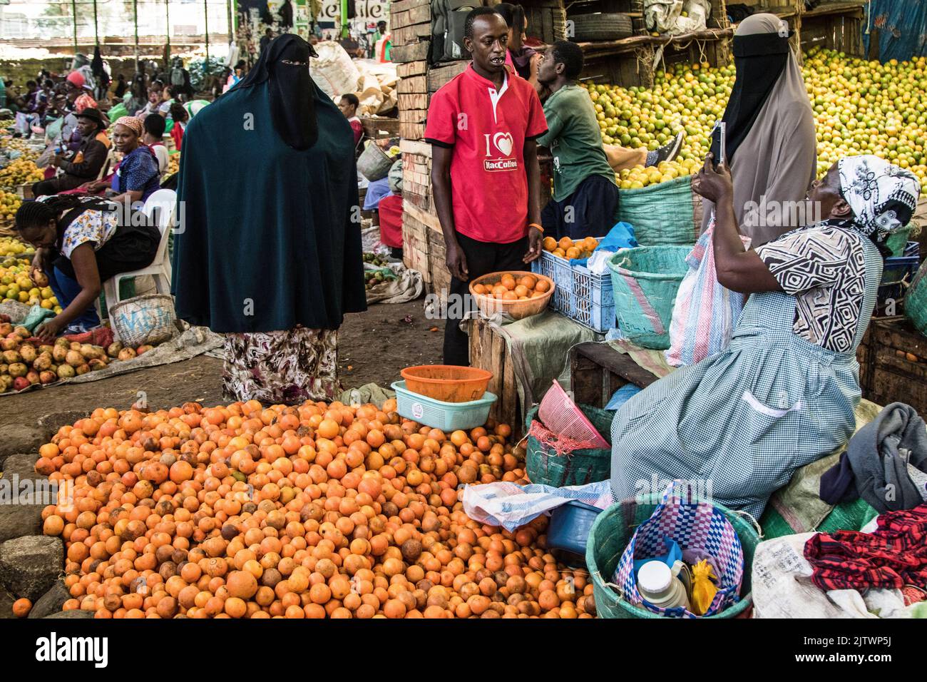 People buy oranges from a trader at a fresh food market in Nakuru Town ...