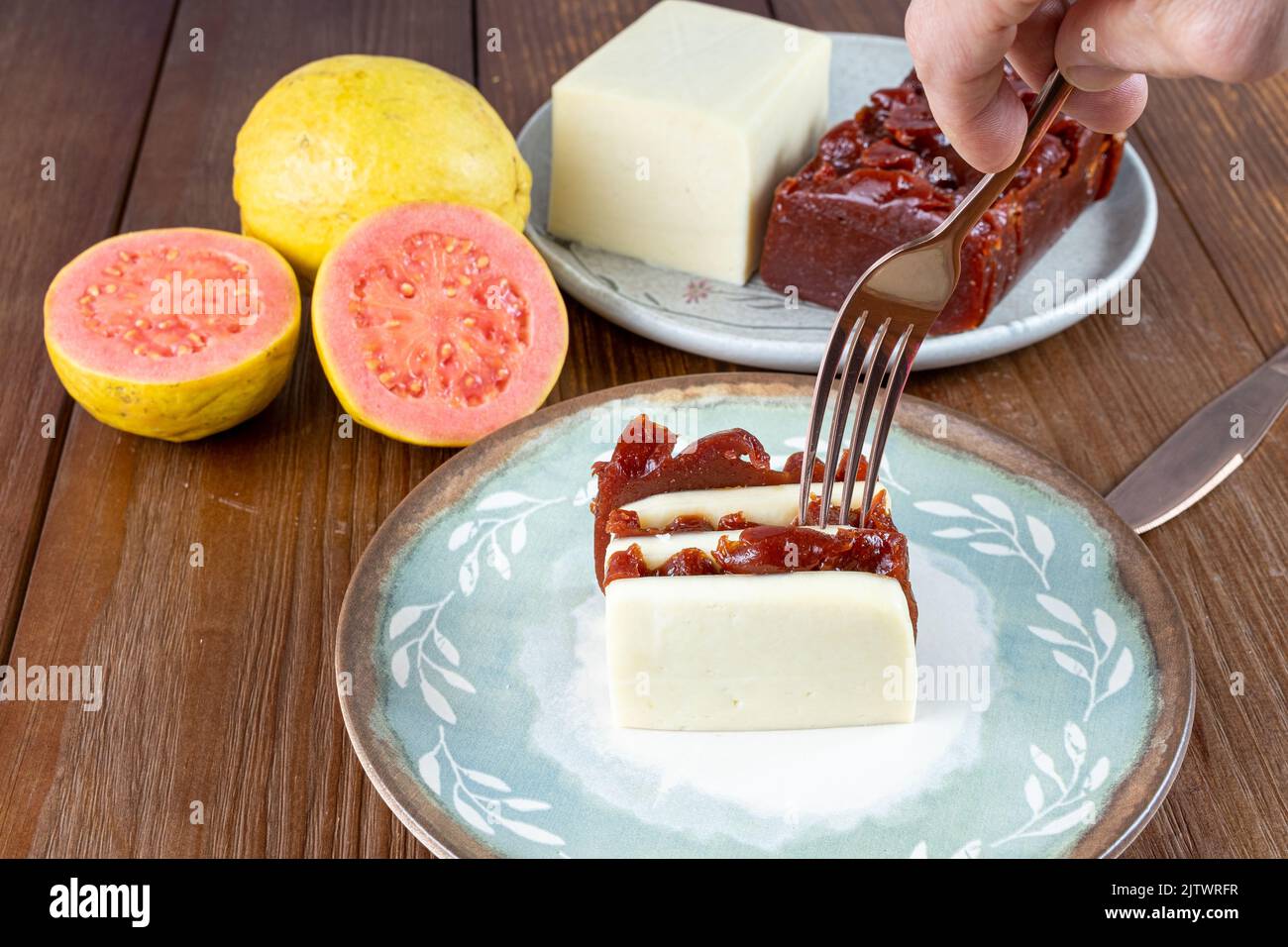Man picking up with a fork, stacked slices of guava sweet and curd ...