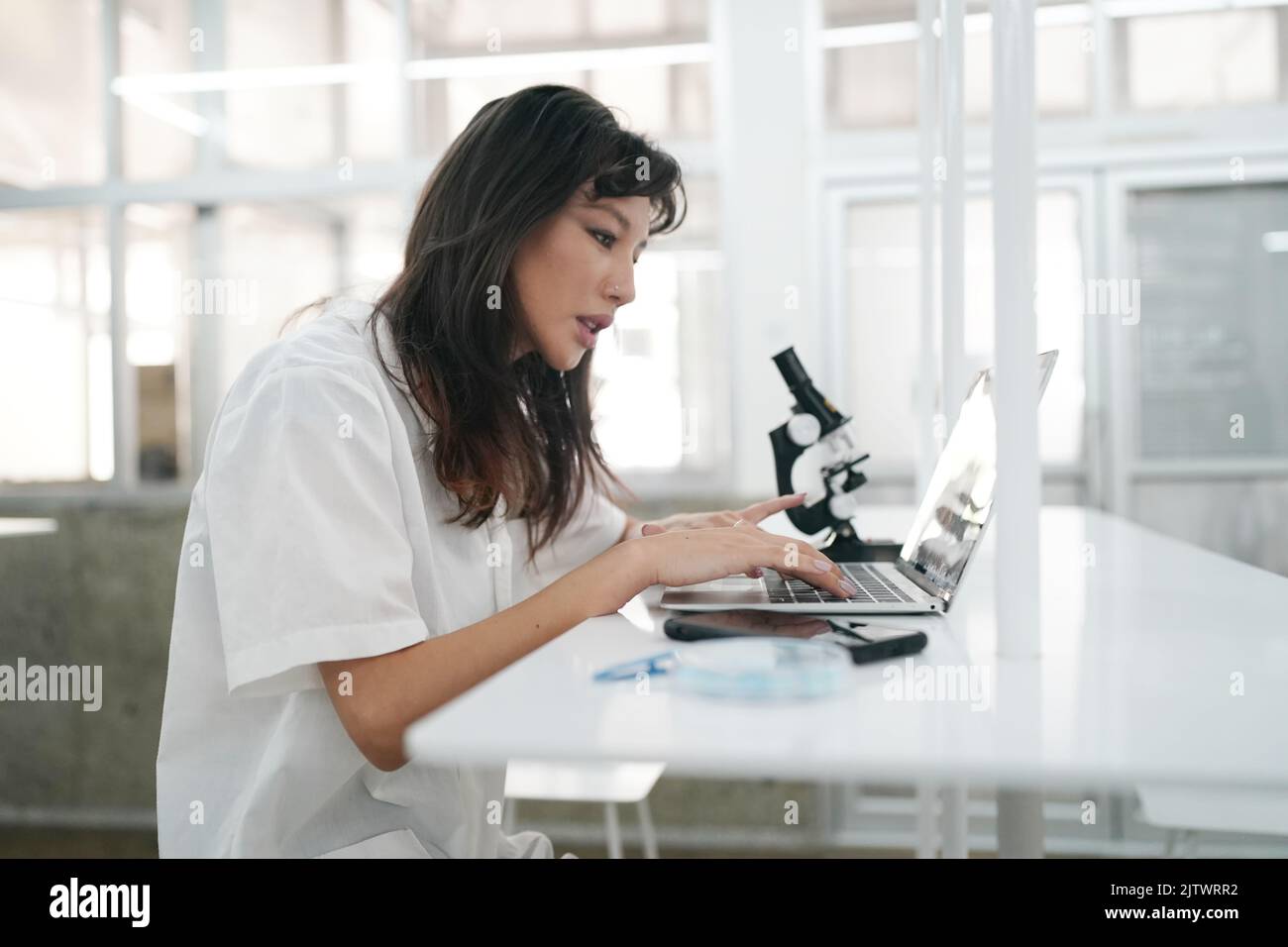 Young scientist in white lab coat working with binocular microscope in ...