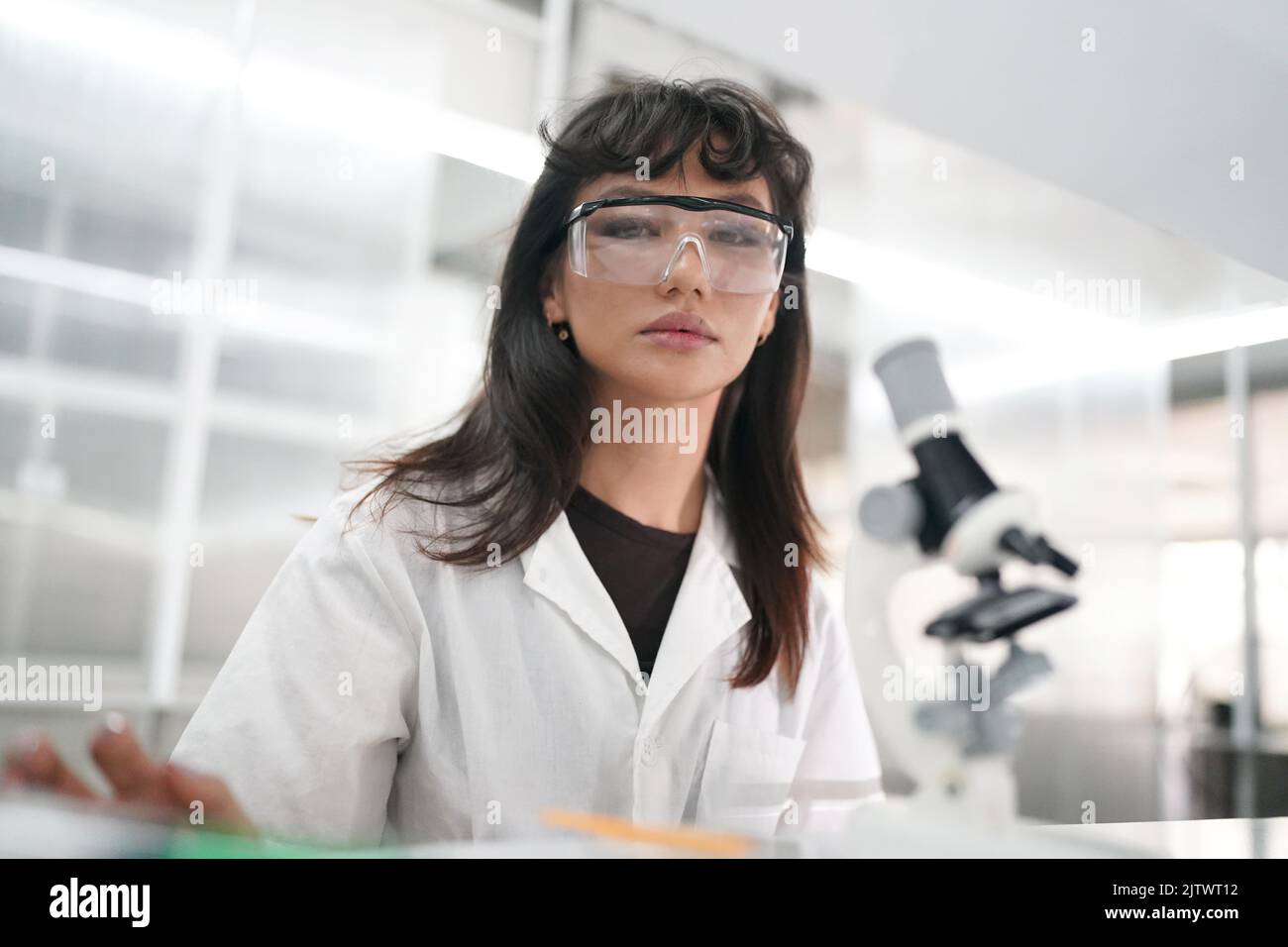 Young scientist in white lab coat working with binocular microscope in ...