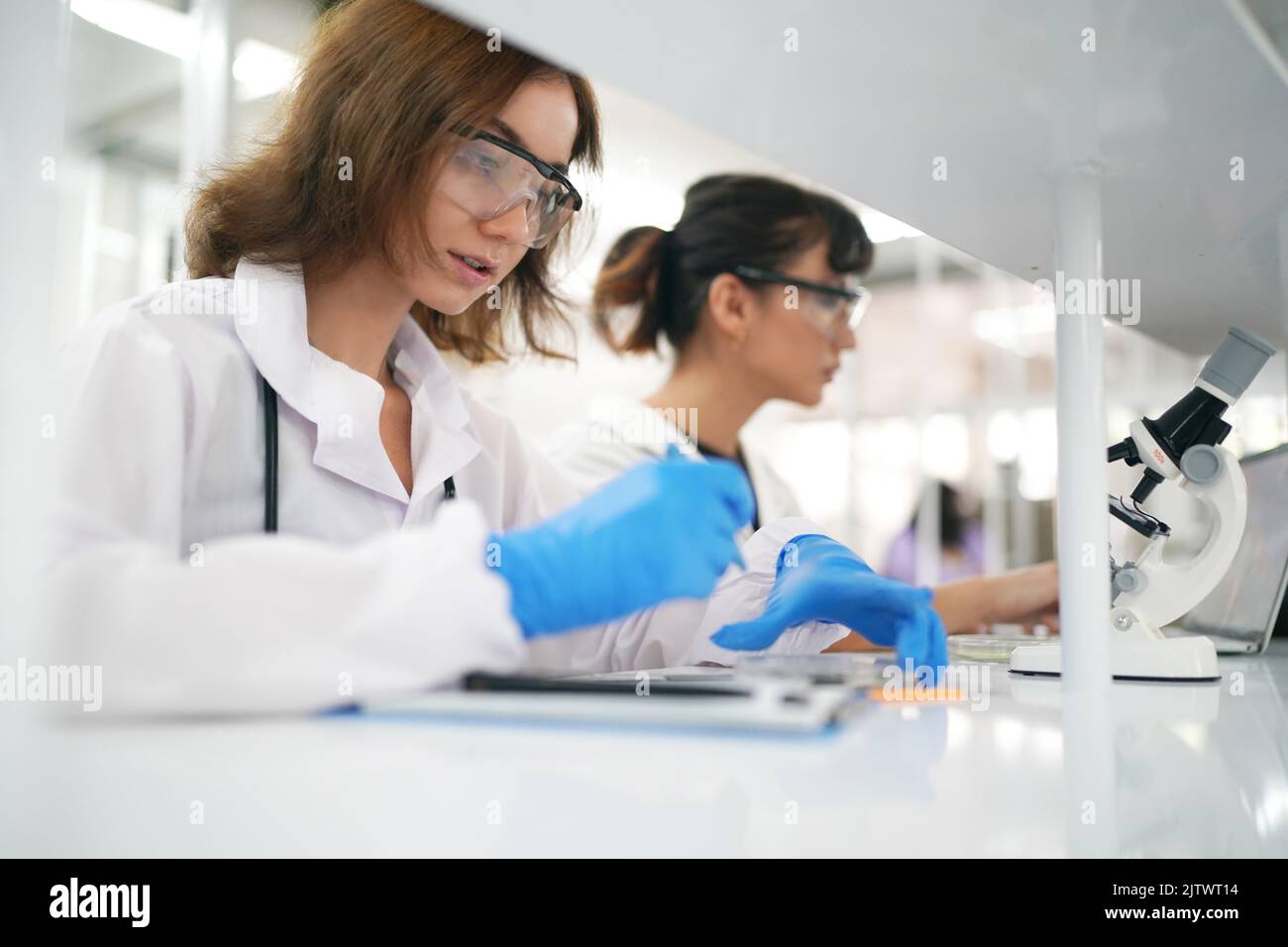 Young scientist in white lab coat working with binocular microscope in ...
